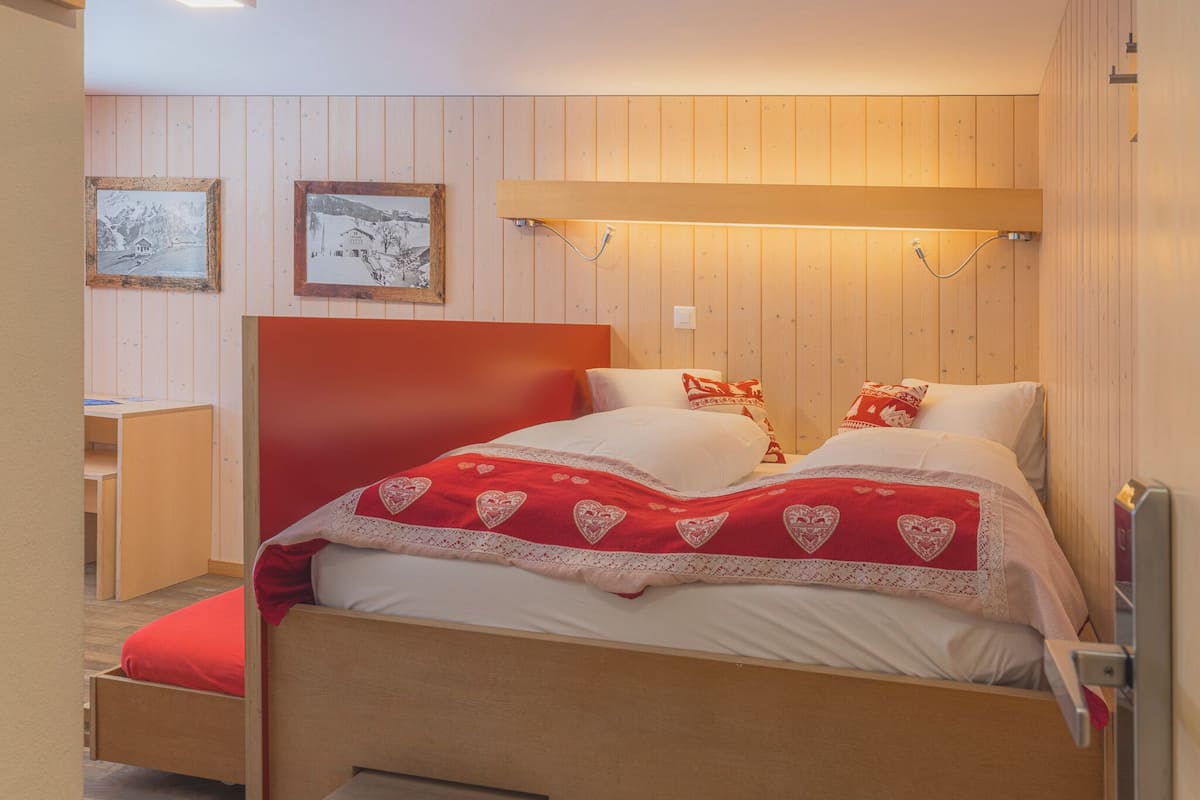 Um quarto com cama de madeira, roupa de cama vermelha e branca, e duas fotografias emolduradas na parede.