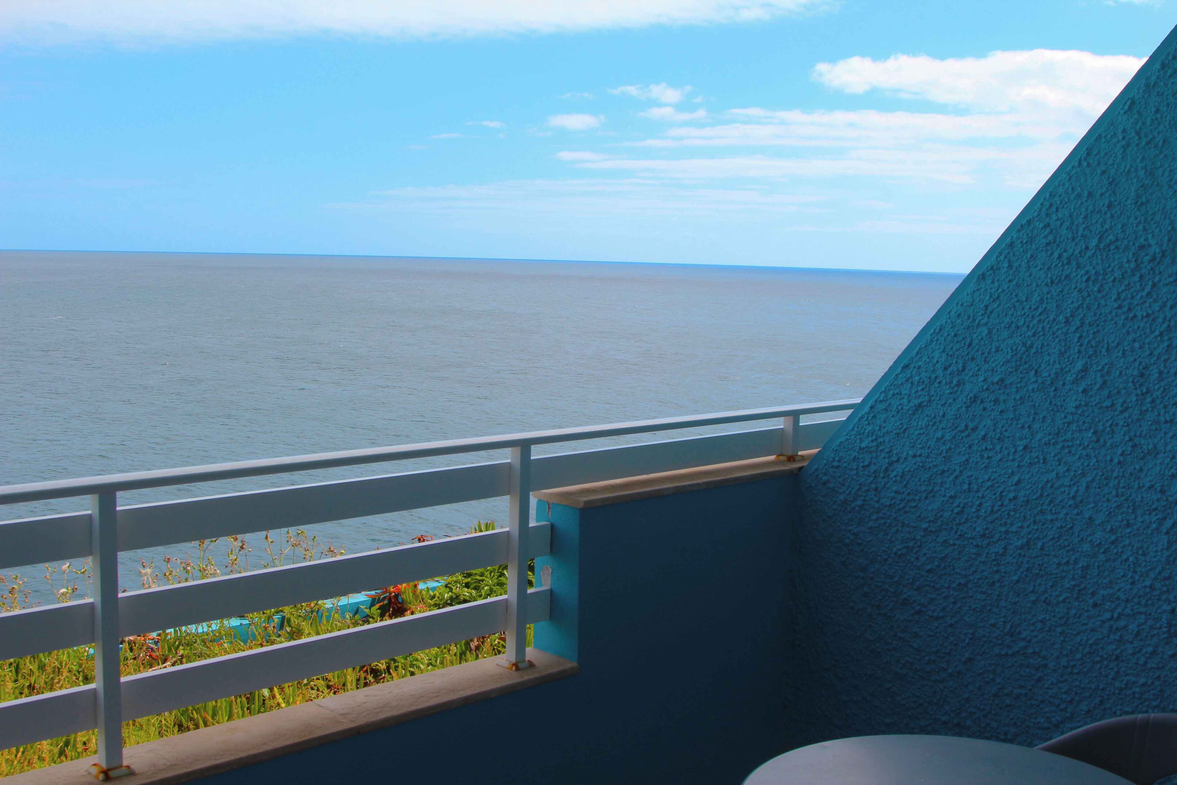 Varanda com vista para o mar, um corrimão e uma parede azul.