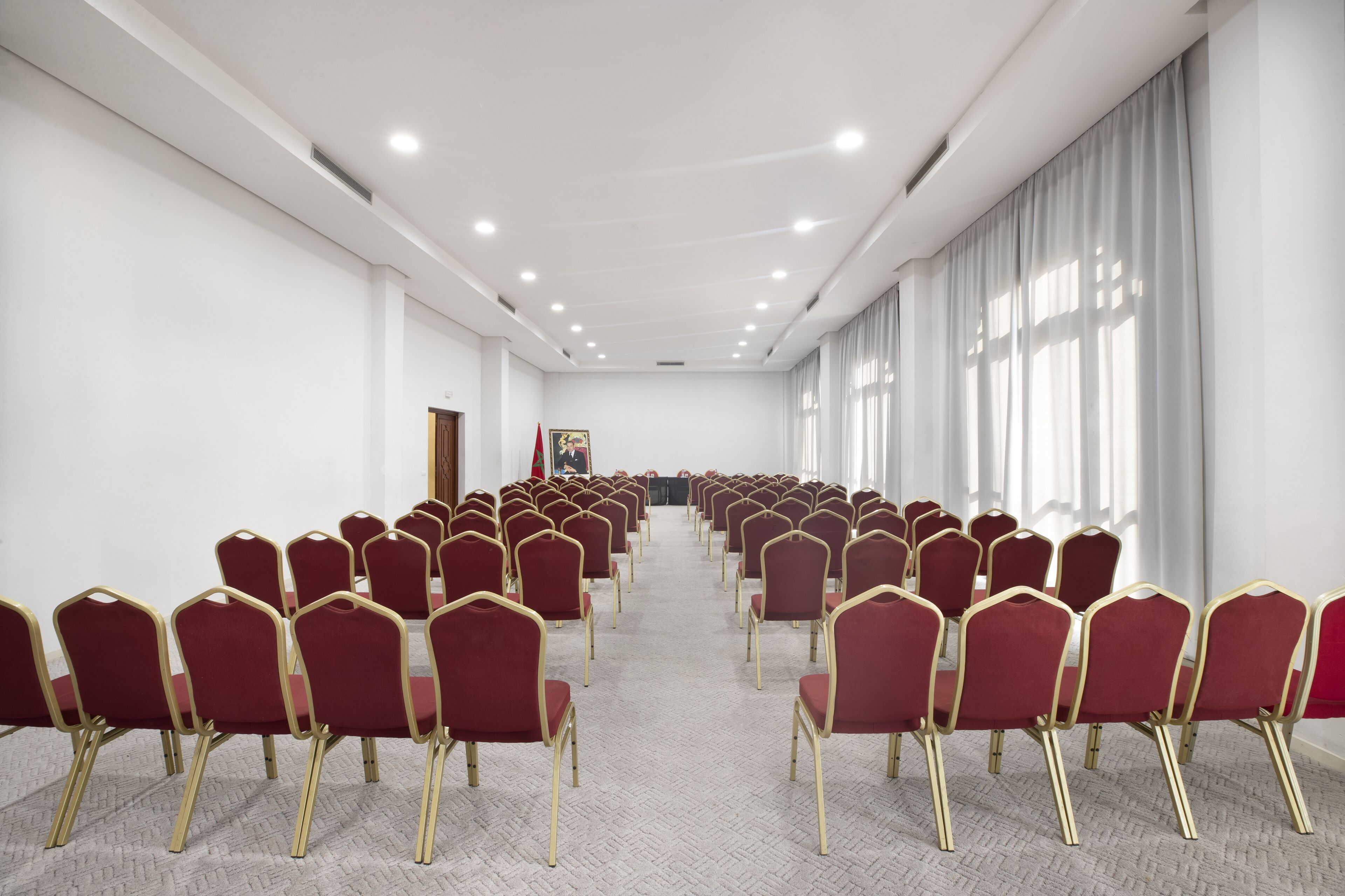 Sala de conferências com fileiras de cadeiras vermelhas e um púlpito na frente.
