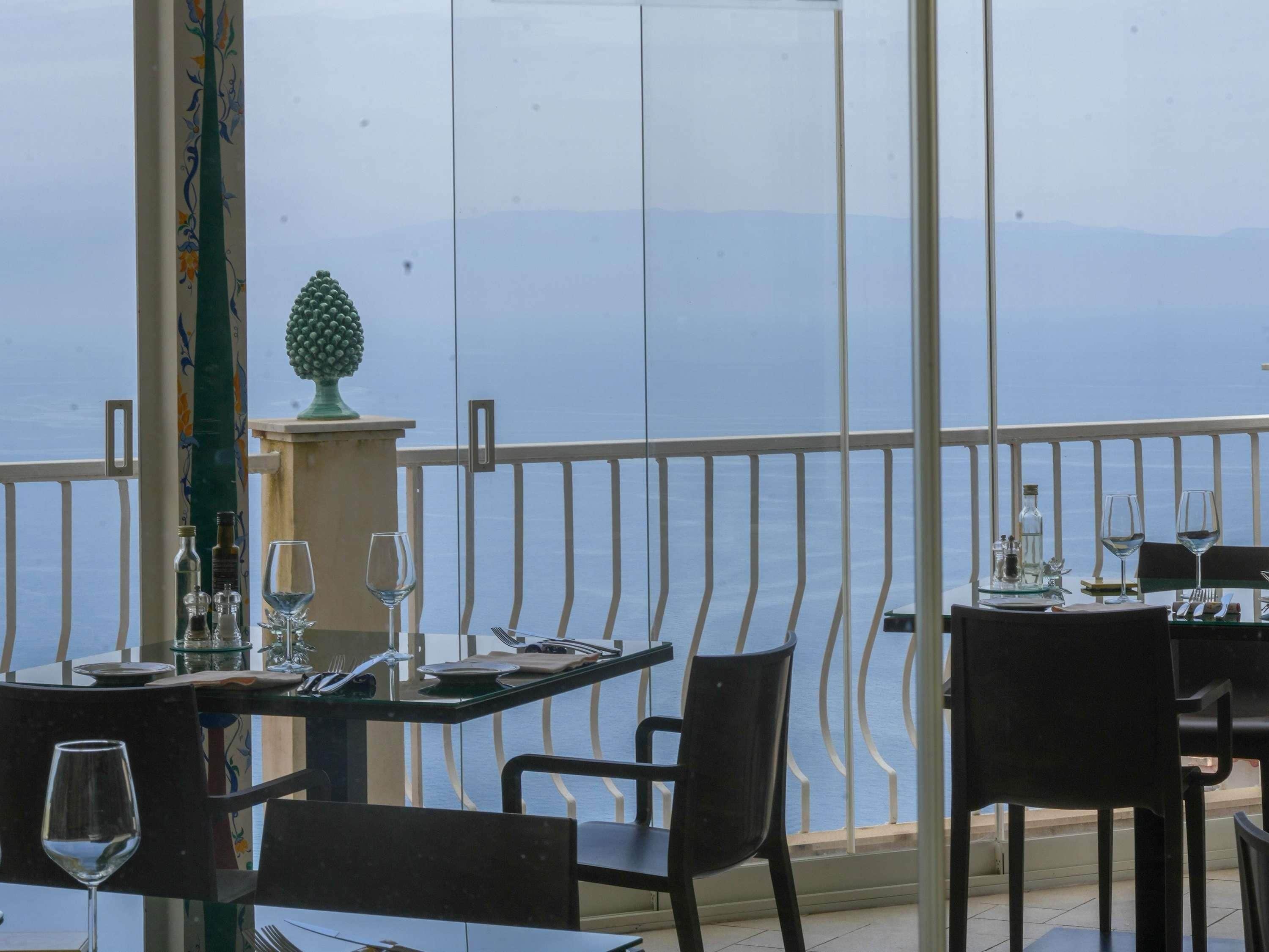 Restaurante com mesas e cadeiras, vista para o mar e uma escultura decorativa de abacaxi.