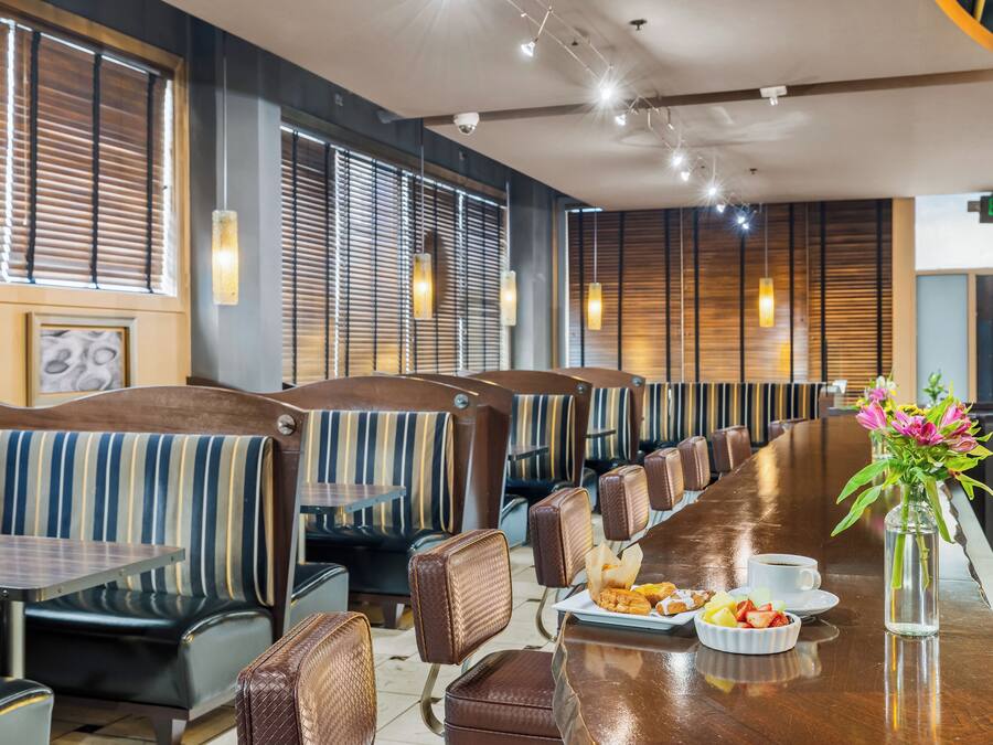 Restaurante com cabines listradas, um balcão comprido com um vaso de flores e um prato de comida.