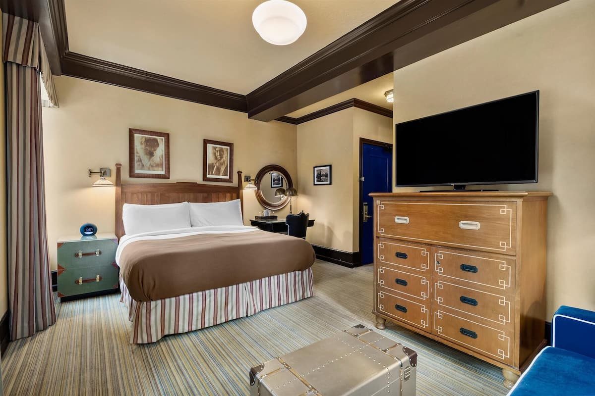 Quarto de hotel com cama, cômoda, televisão e mala.