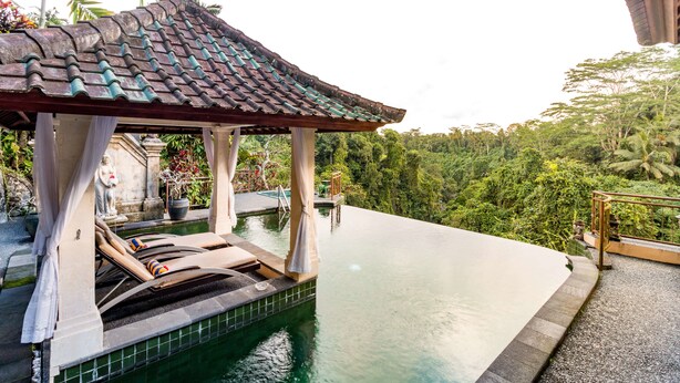 Uma piscina infinita com espreguiçadeiras, um gazebo e uma estátua.