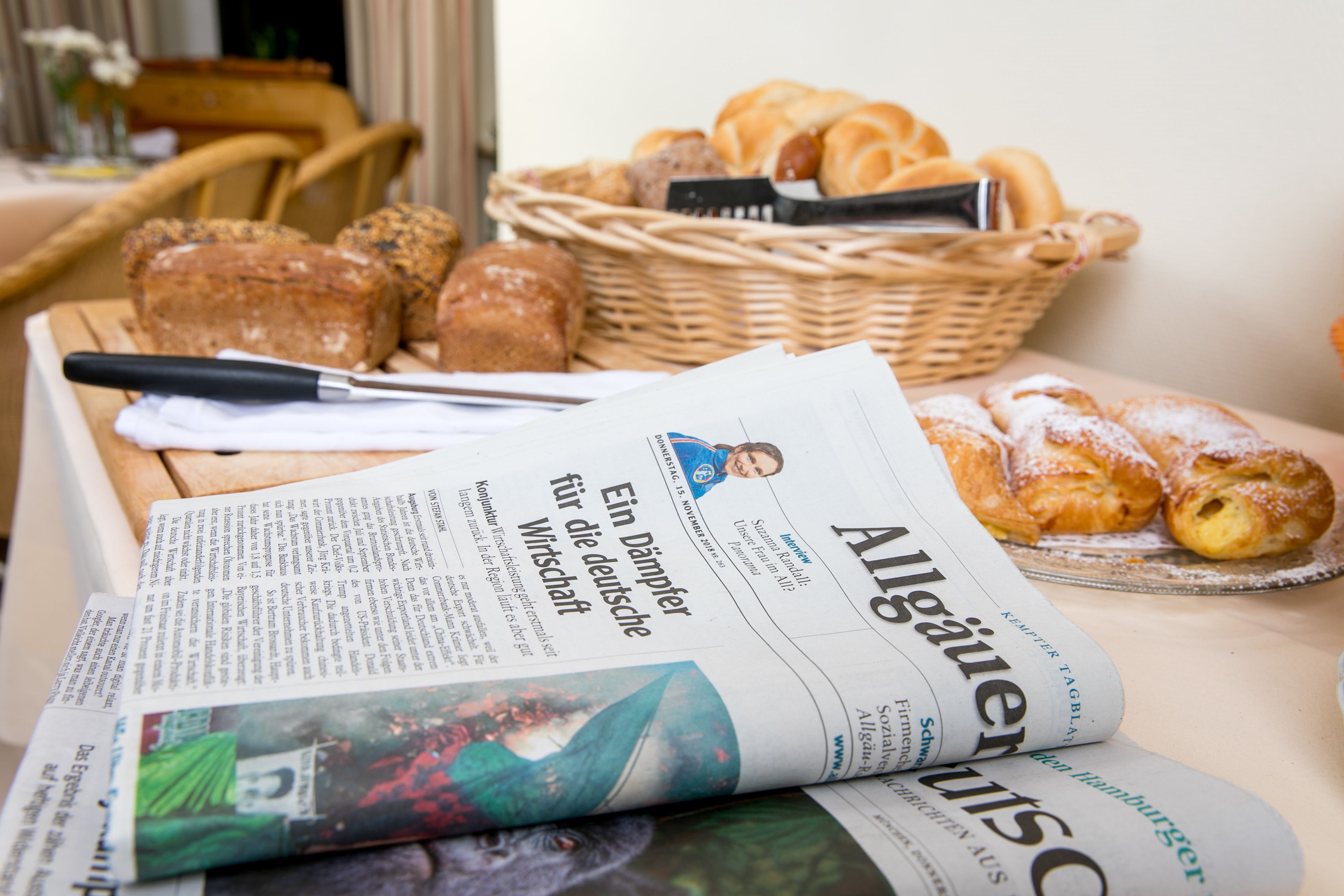 Um jornal aberto sobre uma mesa, com uma cesta de pão e doces.