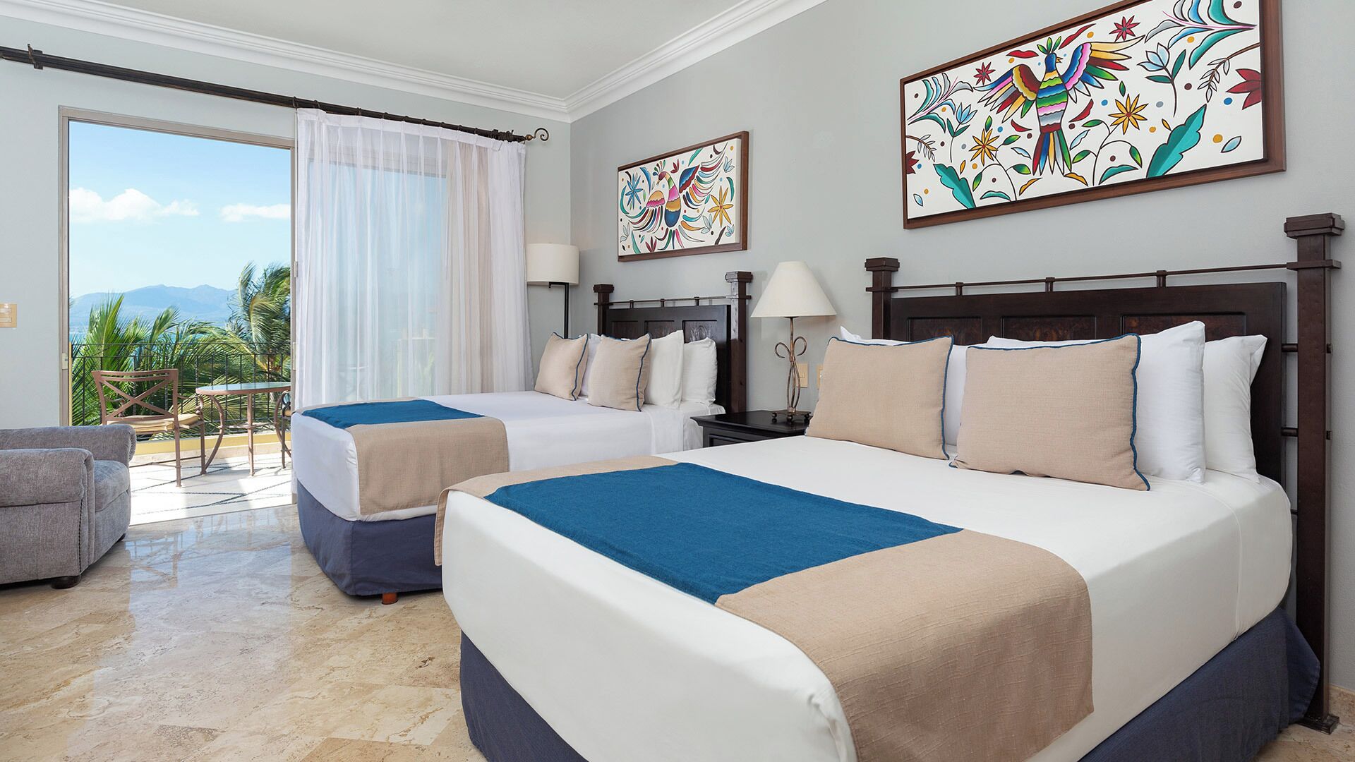 Quarto de hotel com duas camas, varanda e vista, e obras de arte nas paredes.