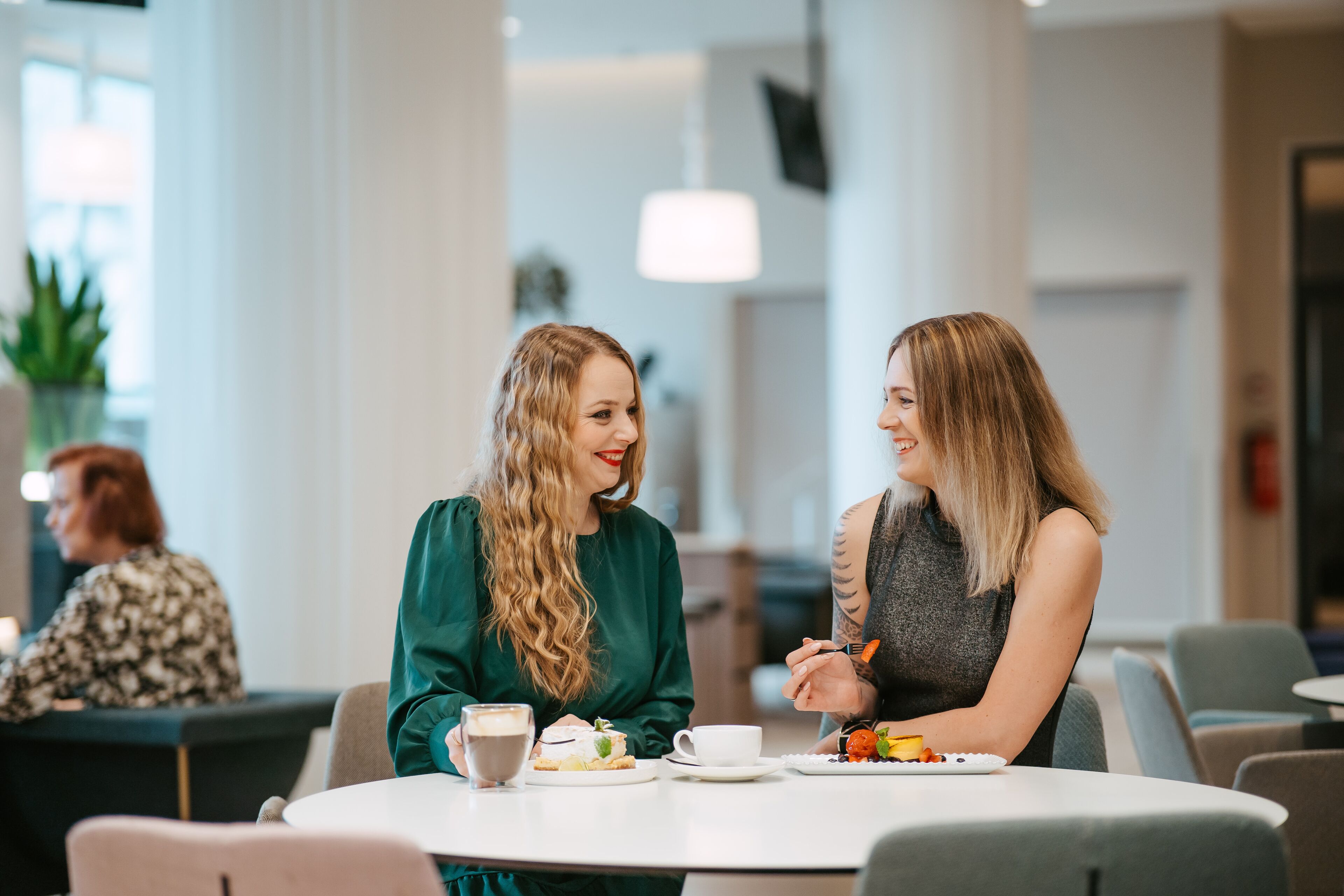 Duas mulheres sentadas em uma mesa redonda em um ambiente interno moderno com cores neutras.