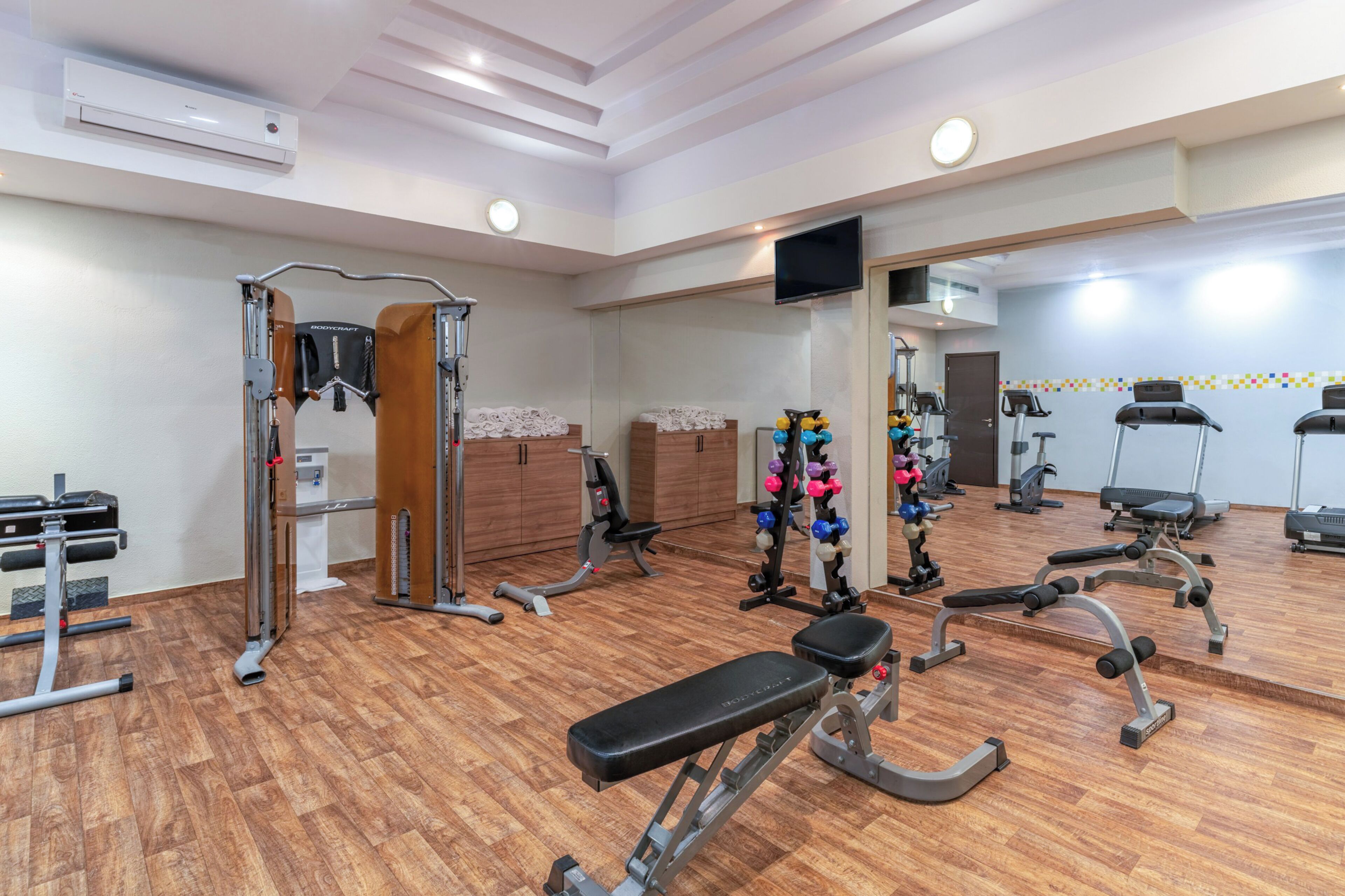Uma academia com diversos equipamentos de exercício, um banco e um painel de espelhos.