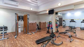Uma academia com diversos equipamentos de exercício, um banco e um painel de espelhos.