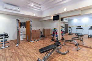 Uma academia com diversos equipamentos de exercício, um banco e um painel de espelhos.