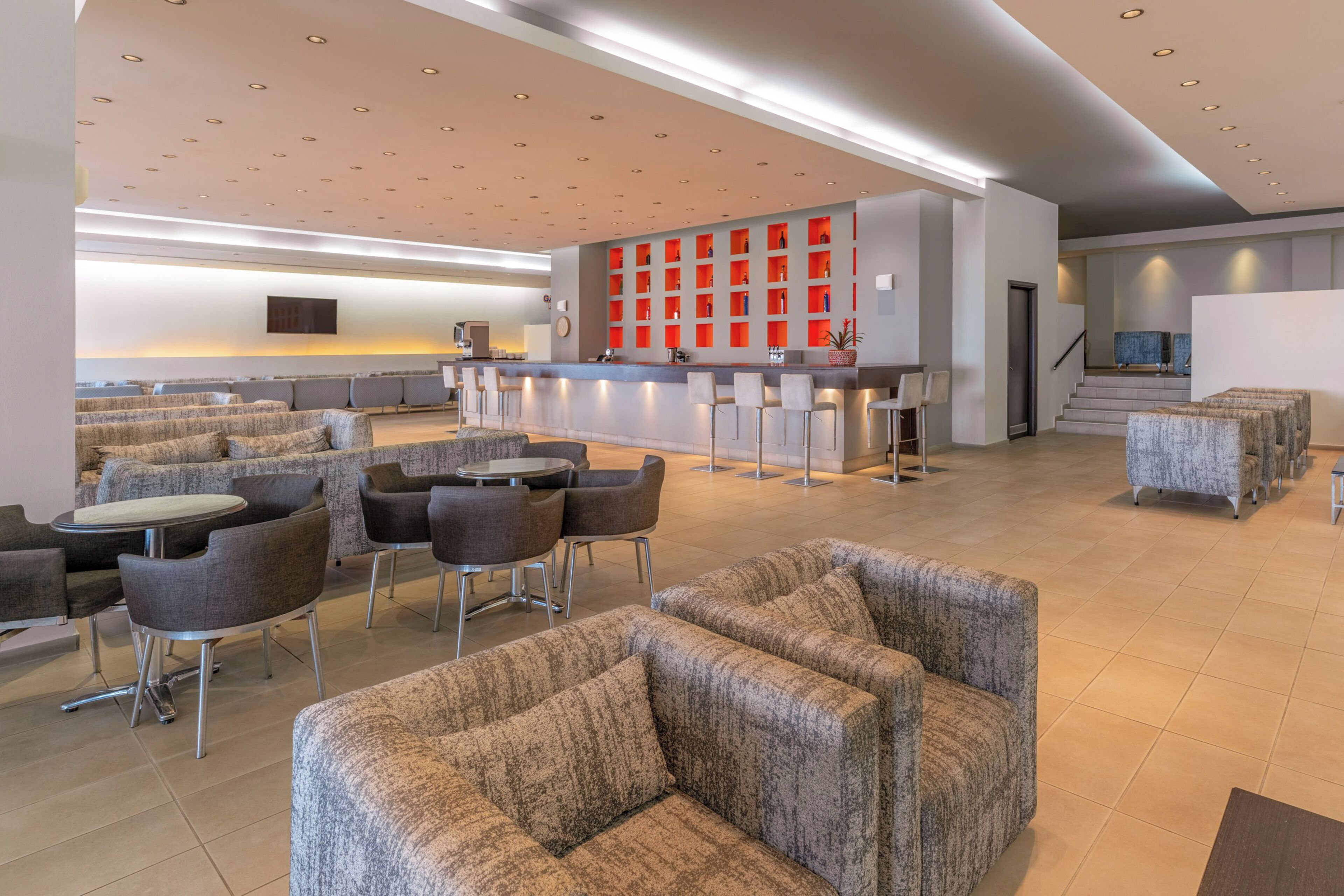 Um hall de hotel moderno com área de bar, espaços de estar e uma escadaria.