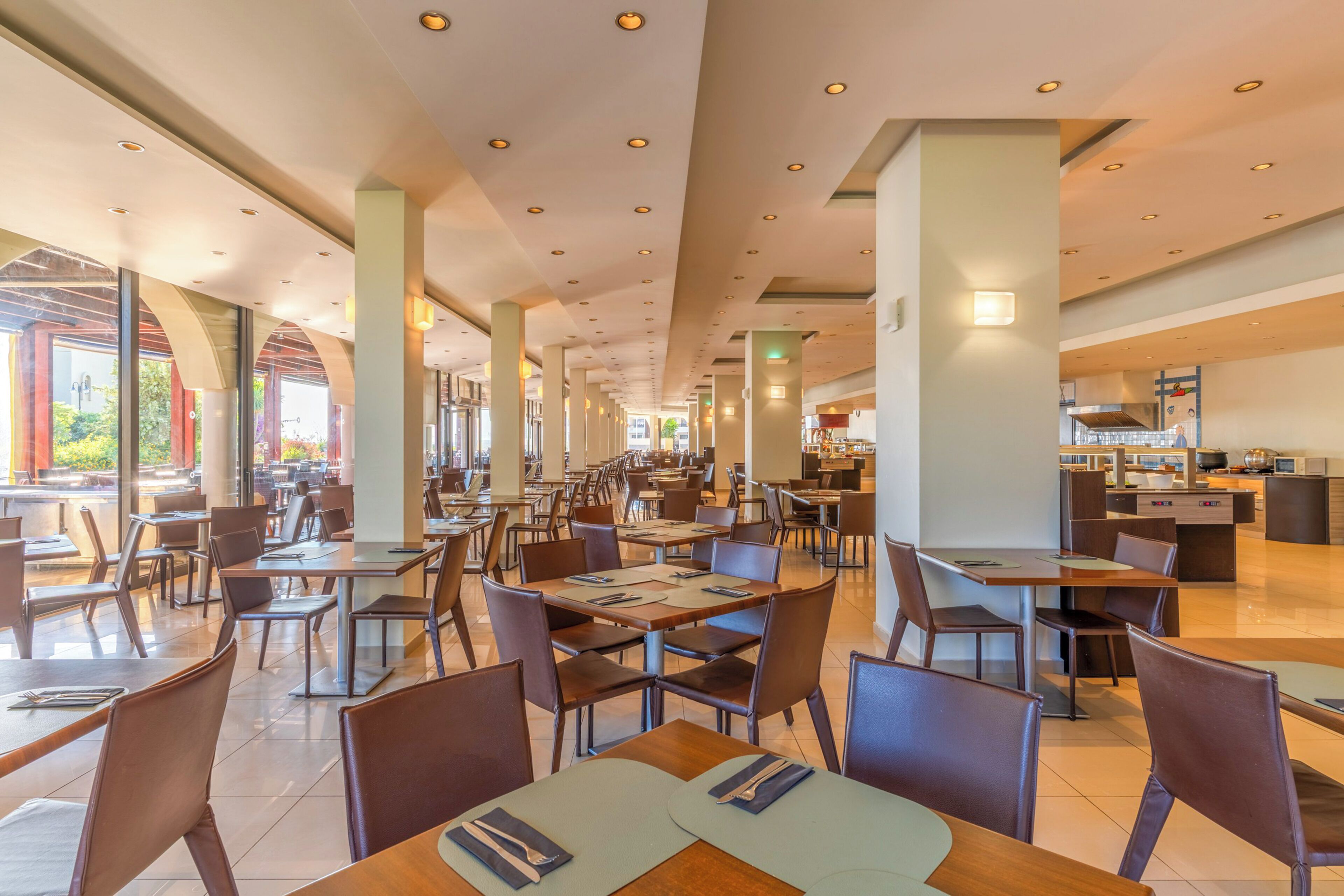Um restaurante espaçoso com várias áreas de refeições, uma cozinha à vista e um amplo espaço aberto com iluminação natural.