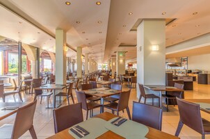 Um restaurante espaçoso com várias áreas de refeições, uma cozinha à vista e um amplo espaço aberto com iluminação natural.