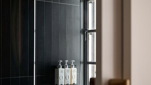 Casa de banho moderna com azulejos escuros, cabine de duche em vidro e janela que proporciona luz natural.