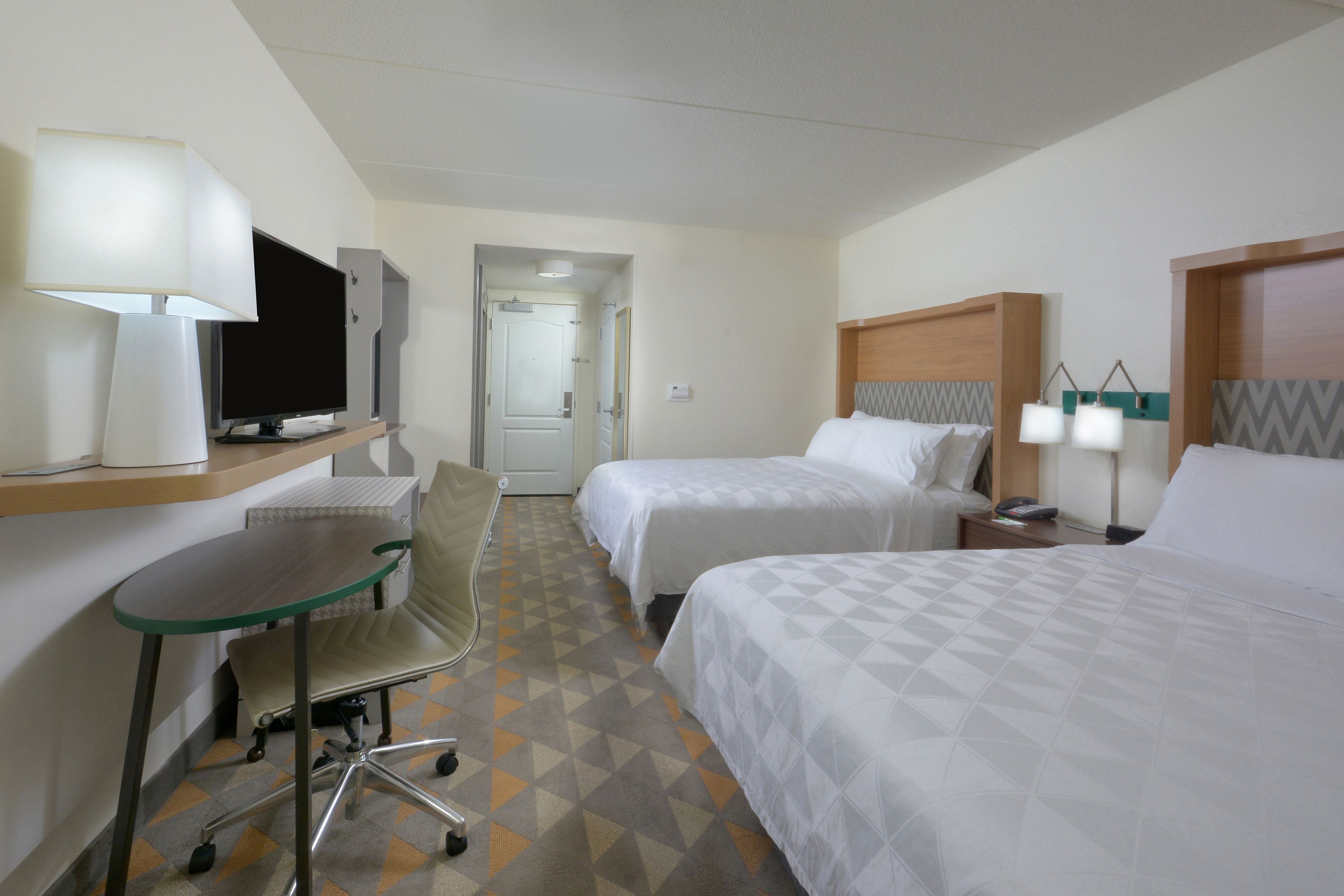 Quarto de hotel com duas camas, uma mesa de escritório com computador, uma cadeira e uma televisão.