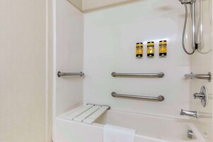 Uma casa de banho moderna com banheira, barras de apoio, porta-toalhas e três frascos de shampoo.