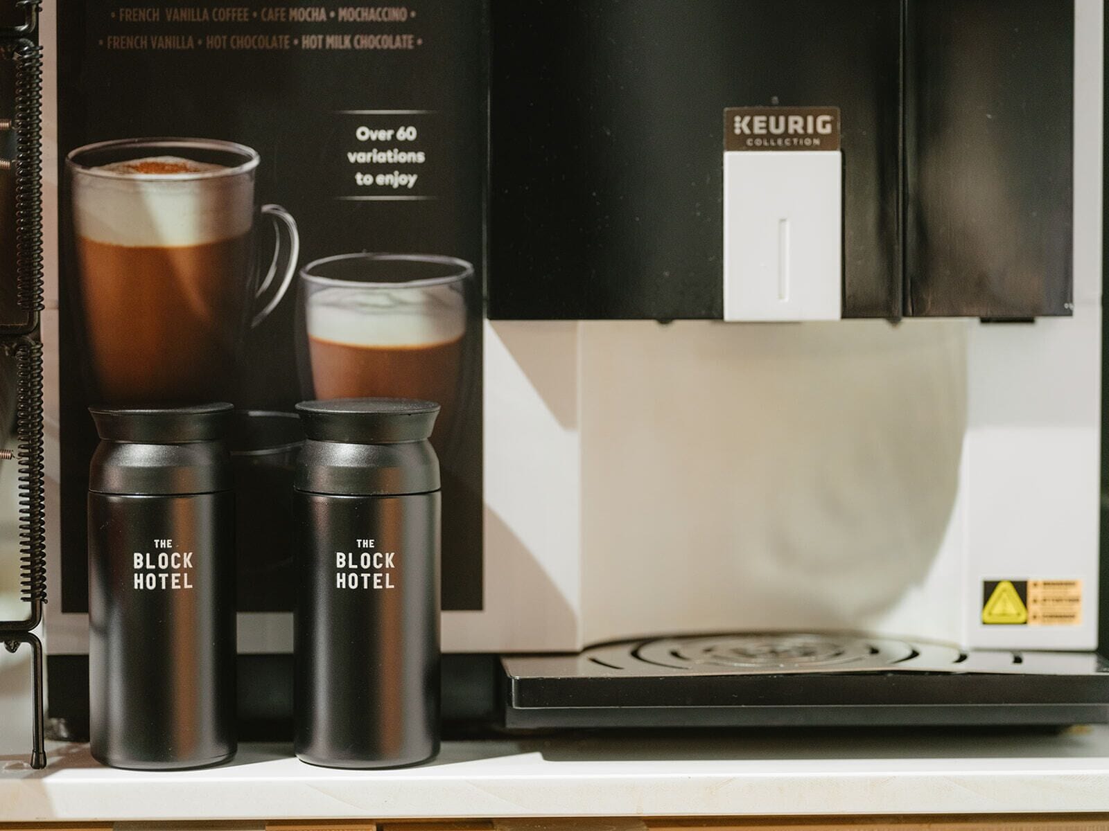 Máquina de café e duas chávenas com a inscrição 'The Block Hotel' numa bancada.