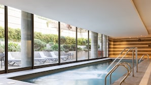 Piscina com vista para o exterior, rodeada por espreguiçadeiras e um muro de pedra.