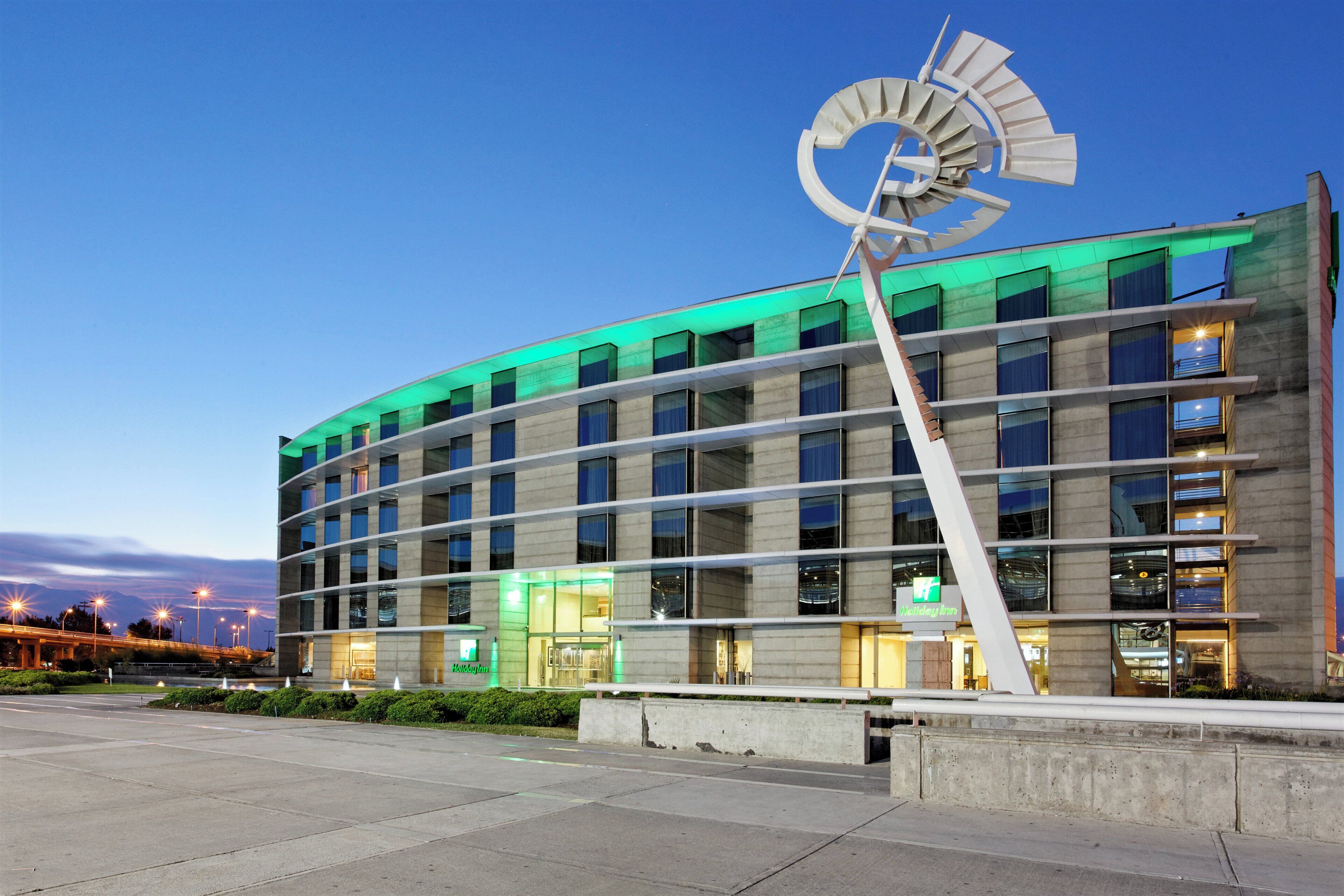 Um edifício moderno com uma escultura espiral marcante na frente, grandes janelas e a placa Holiday Inn.