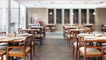 Interior moderno de restaurante, com várias mesas e cadeiras, janelas amplas e obras de arte decorativas na parede.