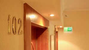 Um corredor com uma porta identificada com o número 102 e uma placa de saída verde na parede.