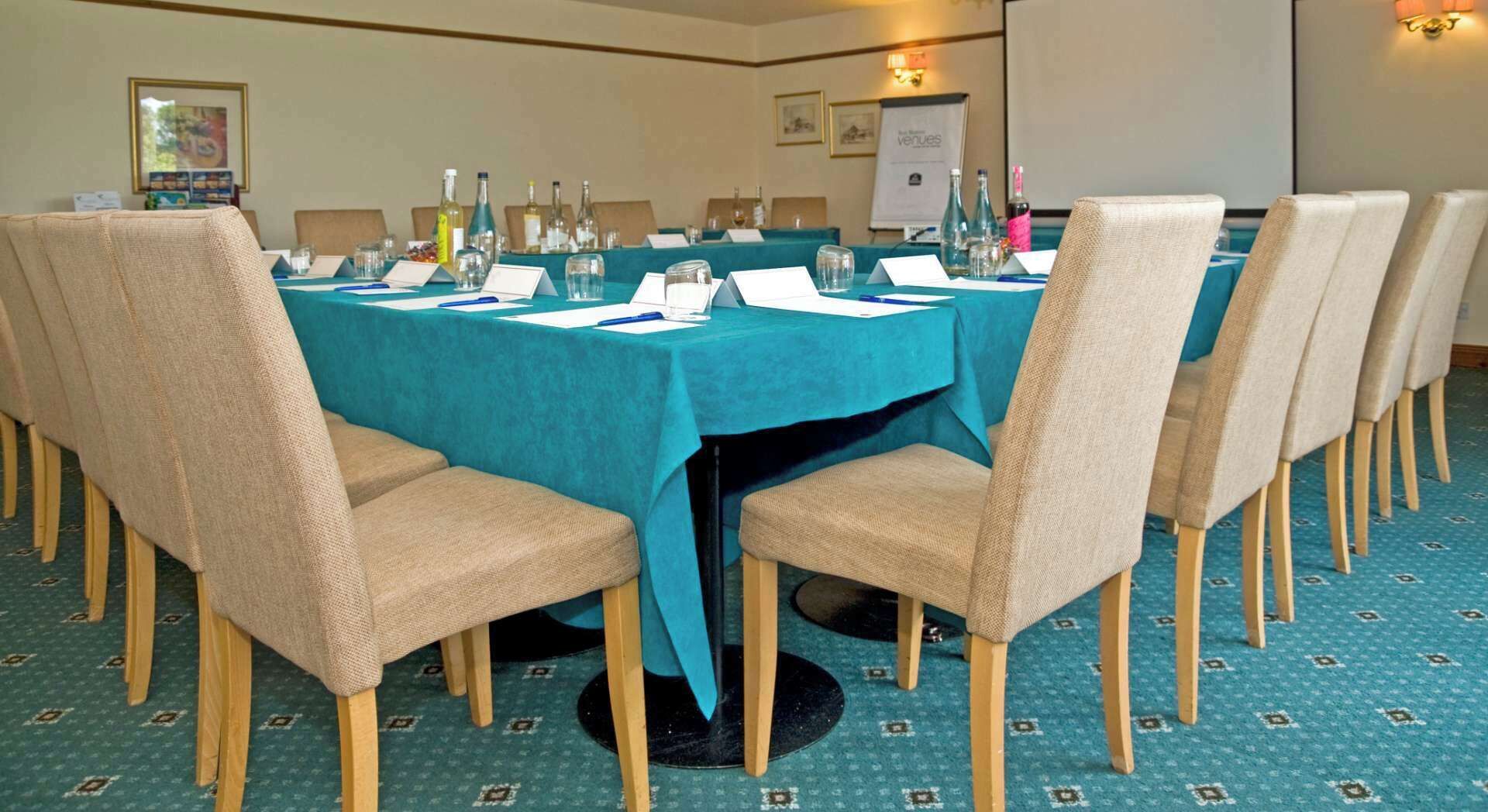 Uma sala de conferências com mesa azul-turquesa, cadeiras bege e carpete estampado.