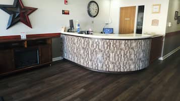 Uma área de recepção com piso de madeira, balcão de recepção com fundo estampado, um relógio e uma decoração em forma de estrela na parede.