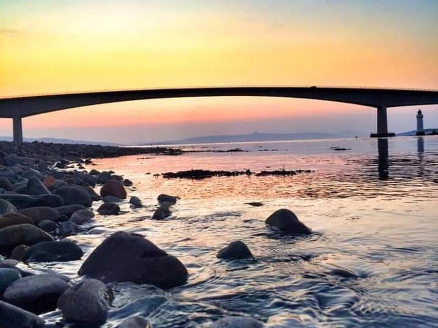 Uma ponte sobre um litoral rochoso, com águas calmas.