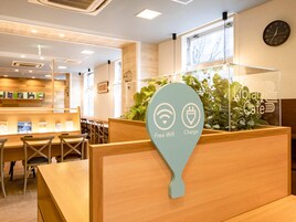 Um café moderno em uma biblioteca, com móveis de madeira, uma planta verde e um aviso indicando wi-fi e carregamento gratuitos.