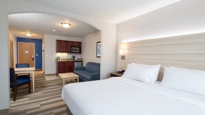 Quarto de hotel com cama, escrivaninha, cadeira, micro-ondas e uma pequena cozinha.