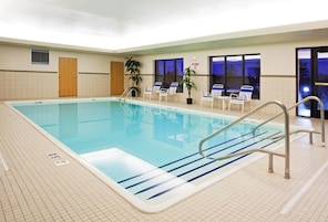 Piscina interior com água cristalina, escada de piscina e espreguiçadeiras.