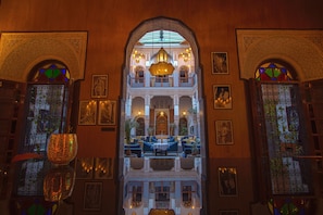 Um hall imponente com área de estar central, arcos ornamentados e um grande lustre.