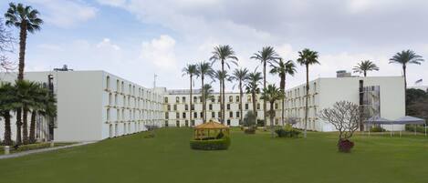 Um hotel com fachada simétrica, várias varandas e um pátio central com palmeiras e um coreto.