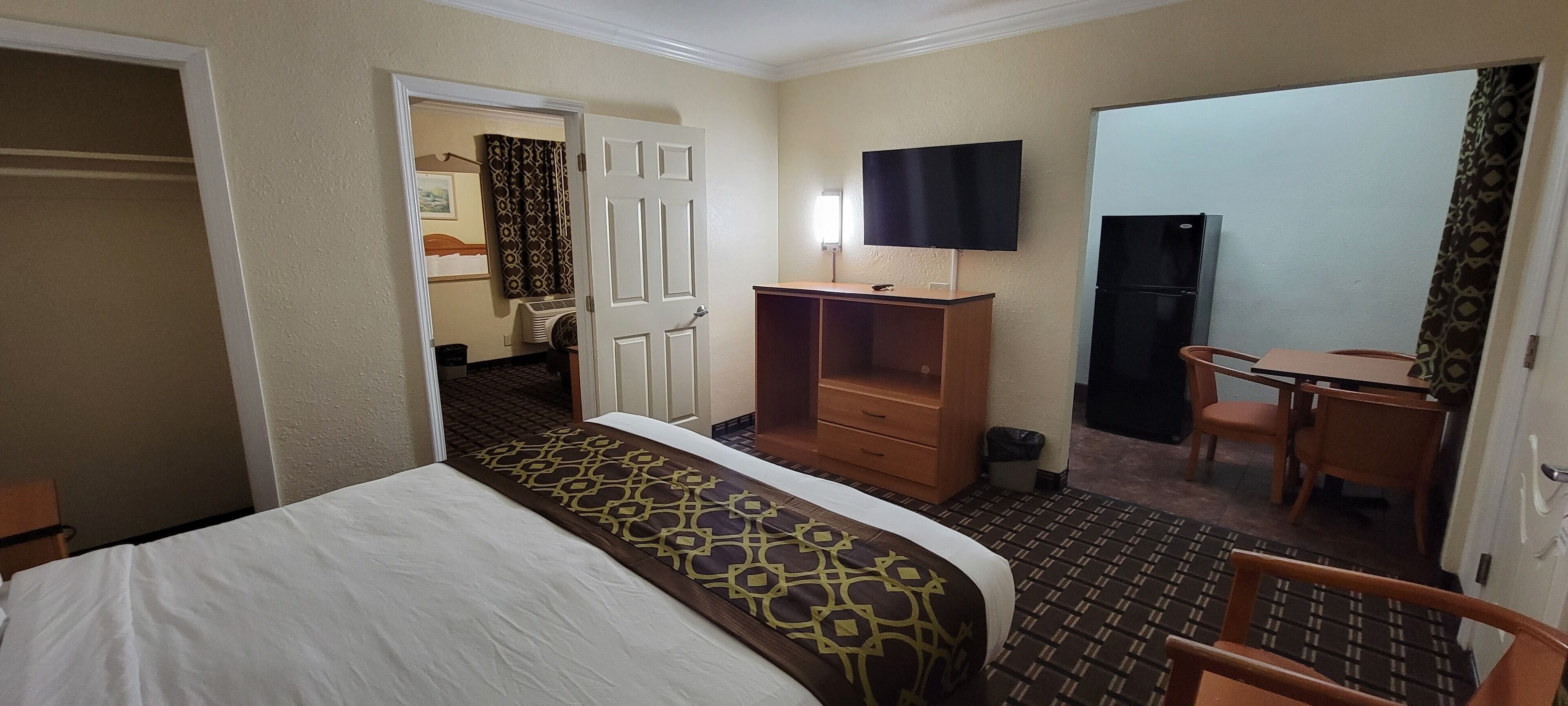 Quarto de hotel com uma cama, uma escrivaninha, uma cadeira, uma televisão e um guarda-roupa.