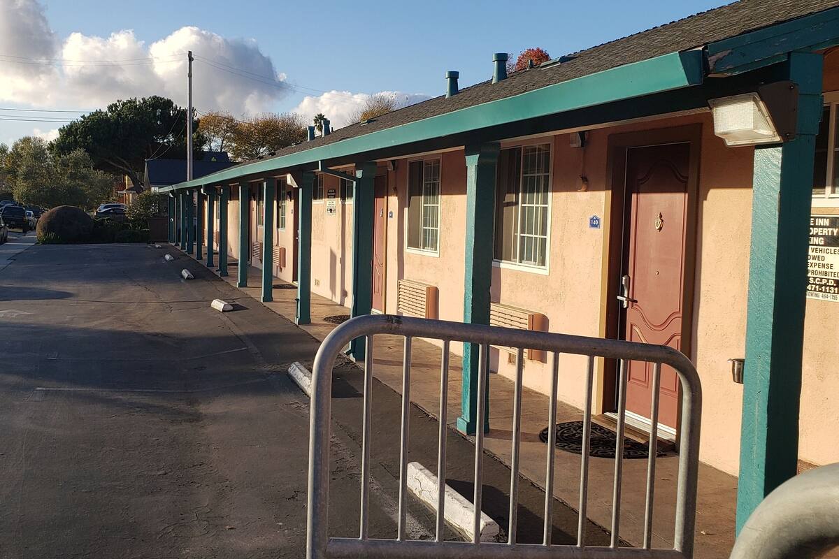 Um motel com uma fileira de quartos, uma placa de limite de velocidade e carros estacionados na rua.