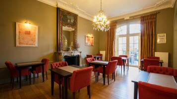 Uma sala de jantar com cadeiras vermelhas estofadas e mesas, um candelabro e uma lareira.