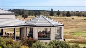 Um edifício moderno com uma estufa de vidro, rodeado por um campo de golfe e uma área arborizada.