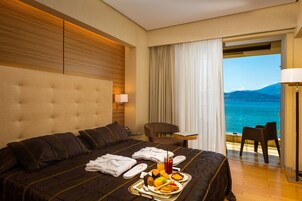 Quarto de hotel com uma cama grande, uma mesa de jantar com café da manhã, uma cadeira e vista para o mar.