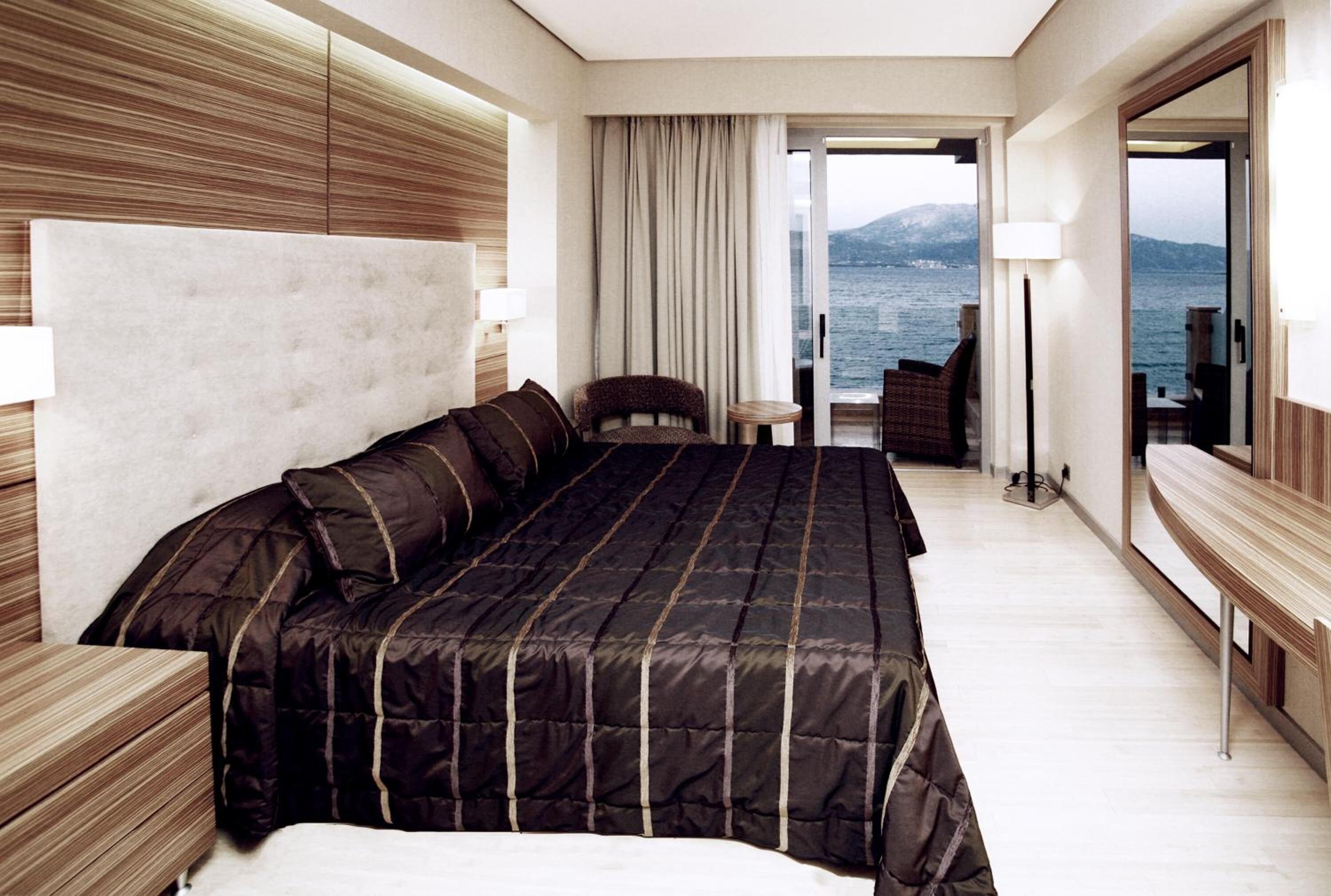 Quarto de hotel moderno com uma cama grande, vista para o mar e varanda com uma cadeira.