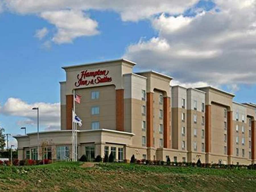 Edifício de um hotel Hampton Inn & Suites com telhado plano, várias janelas e um mastro com a bandeira americana.