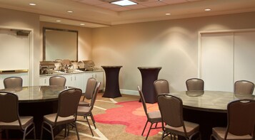 Uma sala de conferências com mesa de vidro, cadeiras, estação de buffet e tapete vermelho.