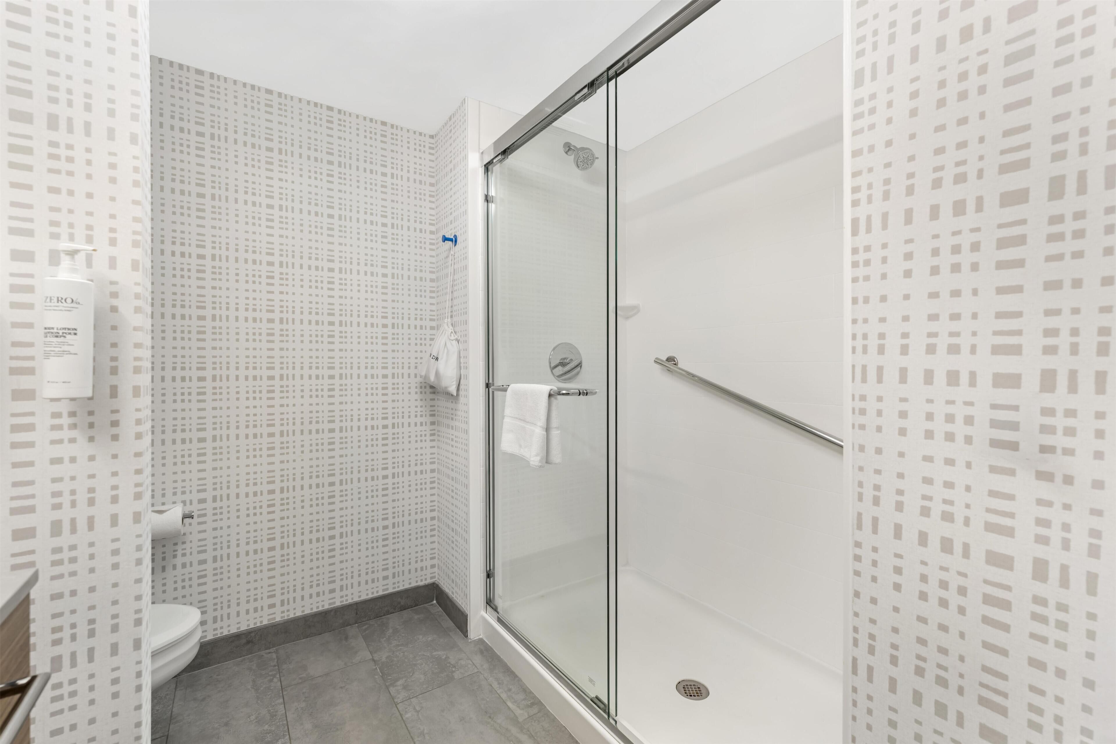 Uma casa de banho moderna com cabine de duche em vidro, sanita e parede com padrão.