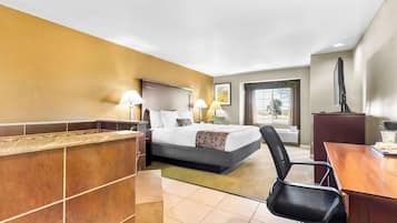 Quarto de hotel com cama, mesas de cabeceira, escrivaninha, poltrona e televisão.