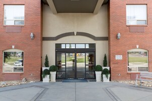 Entrada de hotel com fachada de tijolos, grandes portas de vidro e um banco na parte externa.