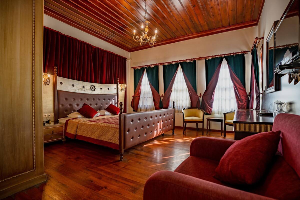 Um quarto com cama, sofá, poltrona, mesa e espelho.