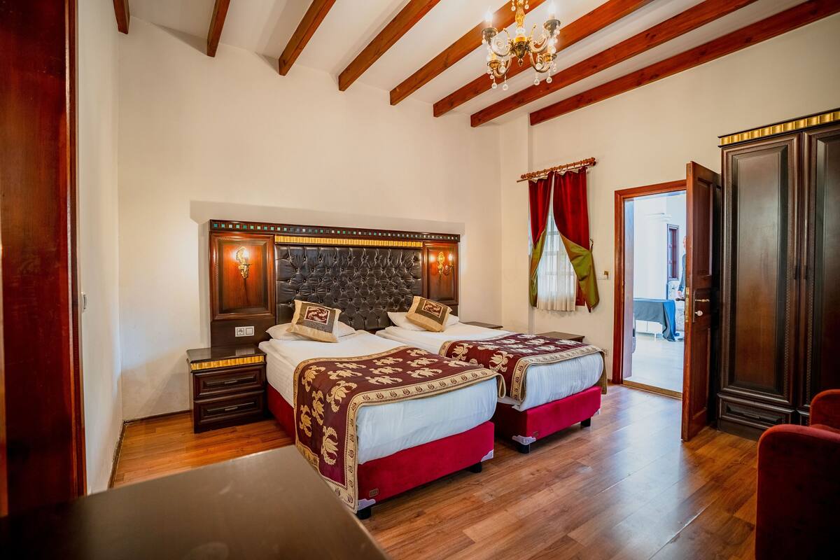 Quarto com duas camas, piso de madeira, um candelabro e um guarda-roupa.