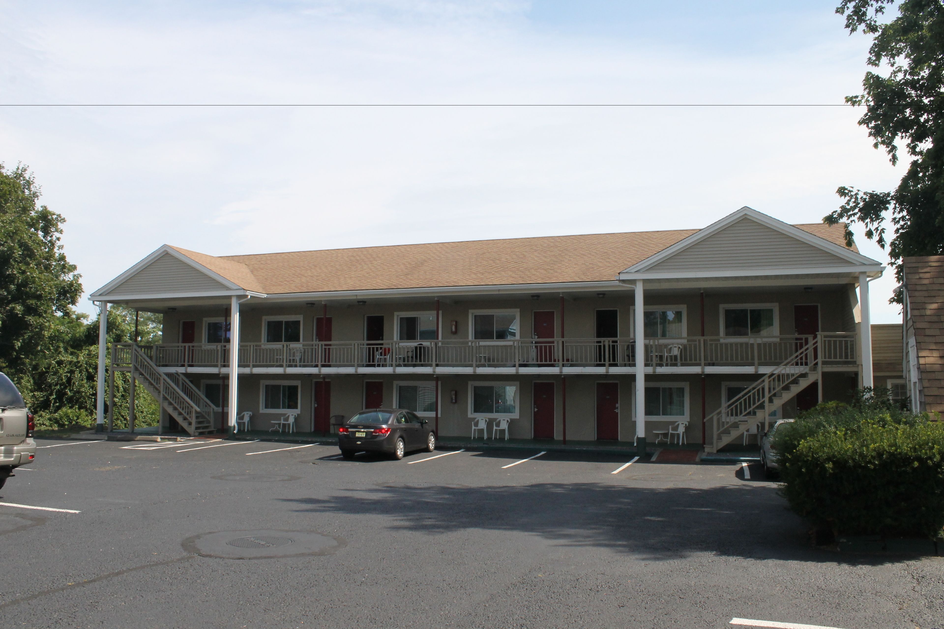 Um motel com estrutura em dois andares, área de estacionamento coberta e um pequeno espaço de estar ao ar livre.