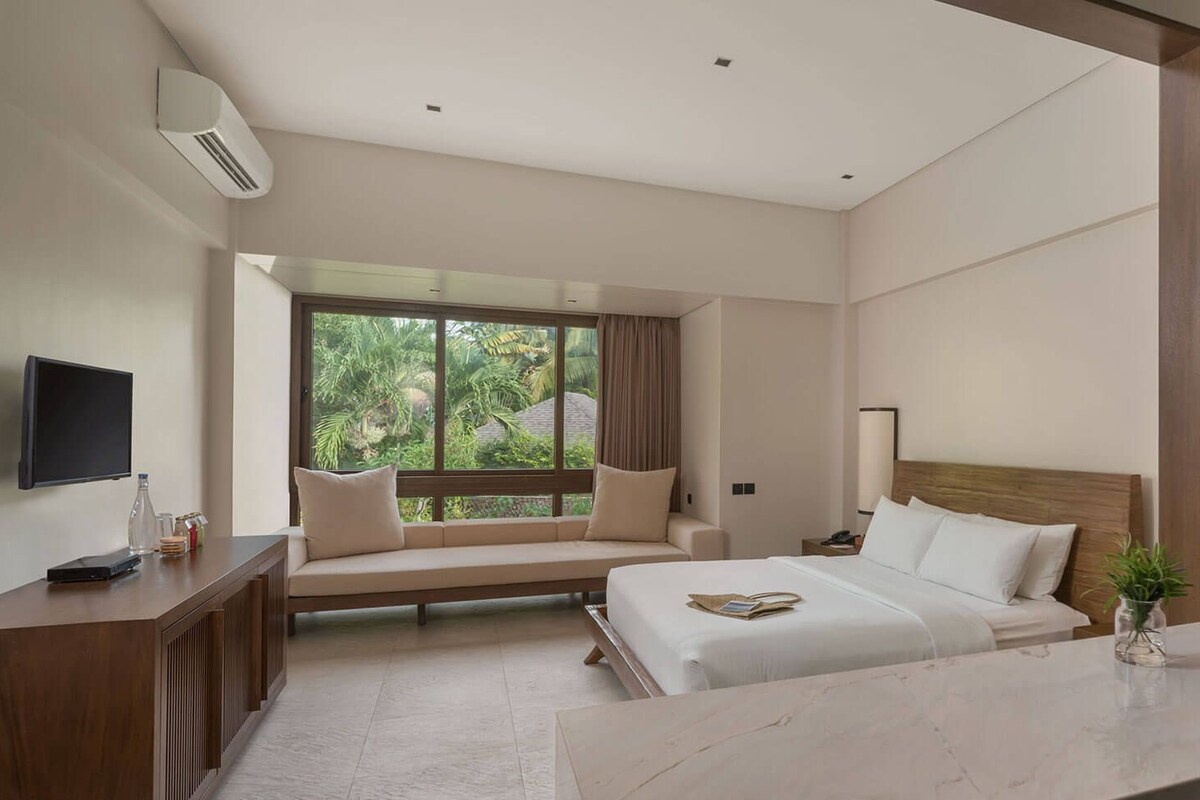 Quarto de hotel moderno com uma cama grande, área de estar, televisão e banheiro com um espelho grande e iluminação.