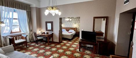 Quarto de hotel com uma cama, uma escrivaninha com cadeira, televisão e sofá.