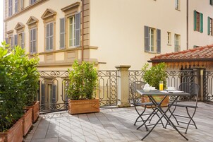 Um terraço com mesa, cadeiras, plantas em vasos e um corrimão.