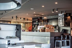 Uma área de bar com balcão, prateleiras de garrafas e banquetas.